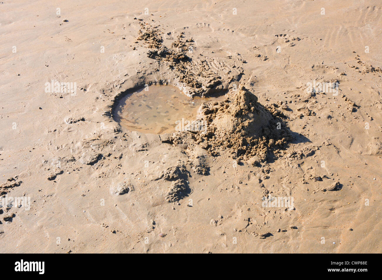 Sand piled up and destroyed on sandy beach, leaving circular pool, hand ...