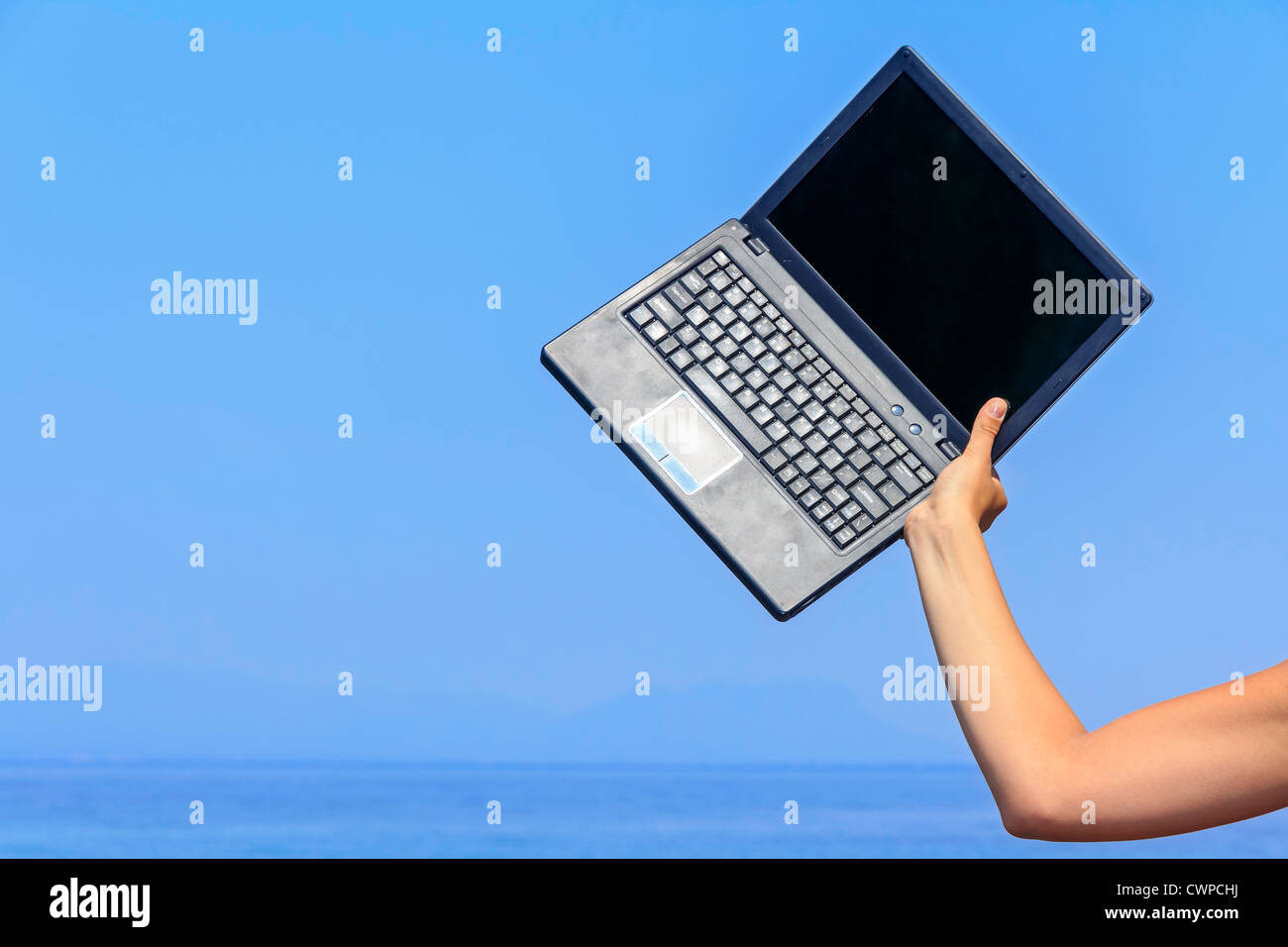 Hand holding a laptop at sea against a blue sky Stock Photo - Alamy