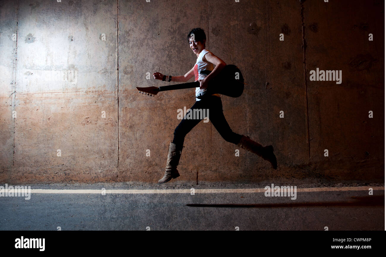 dark grunge style asian rock star jumping and holding a guitar Stock ...