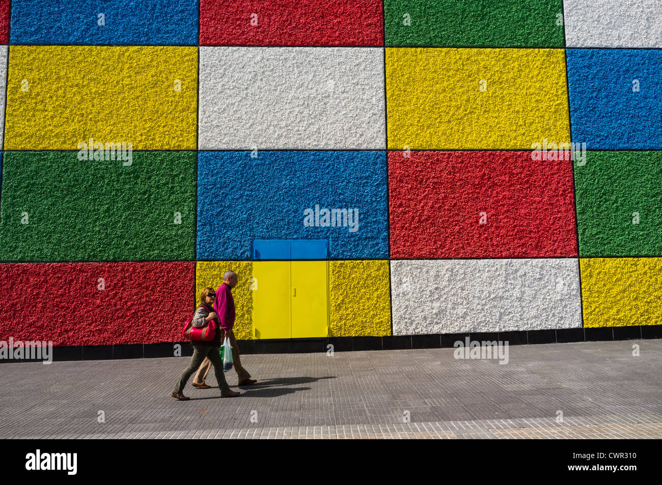 A couple walk past a brightly painted shopping mall in Benidorm, Spain ...