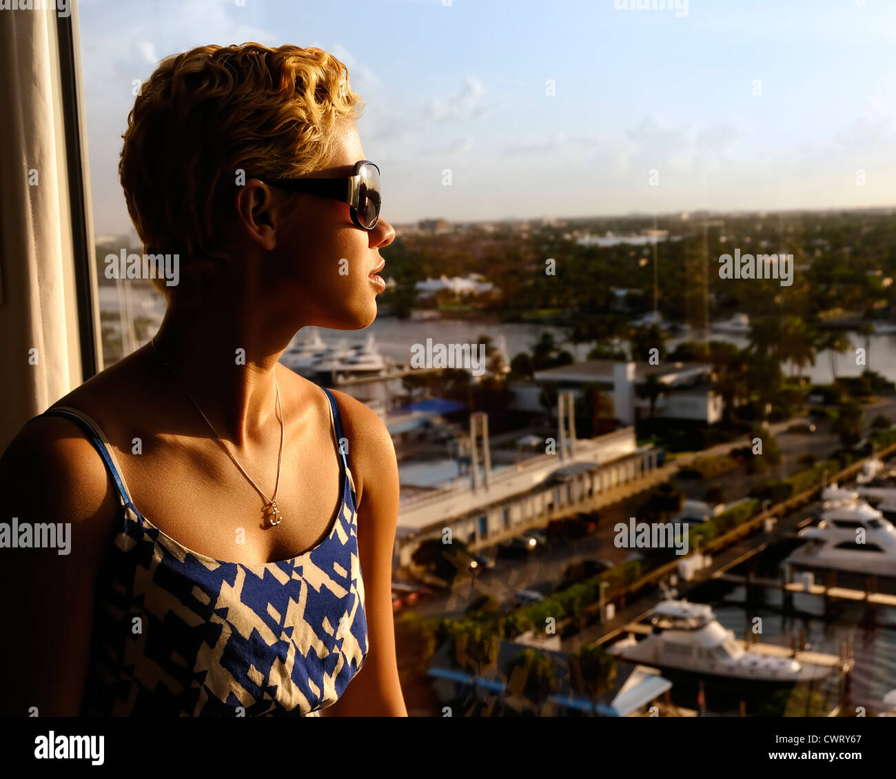 Girl wearing sunglasses looking out of a hotel window in Ft Lauderdale ...