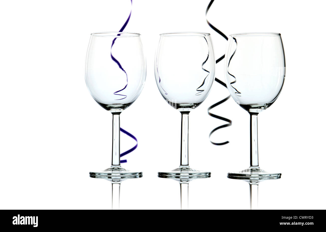 Three empty wine glasses and party streamers back lit against white ...