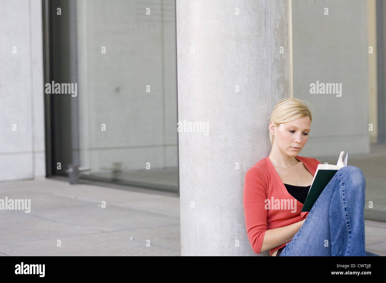 Young woman leaning against column reading book Stock Photo - Alamy