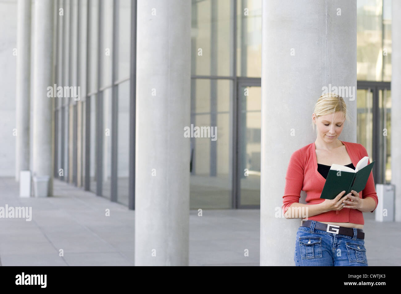Young woman leaning against column reading book Stock Photo - Alamy