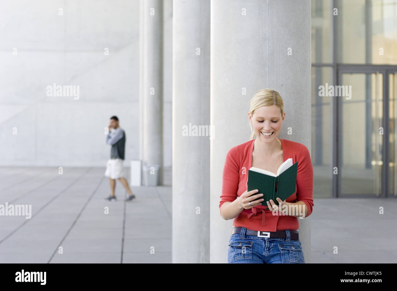 Happy young woman leaning against column reading book Stock Photo - Alamy