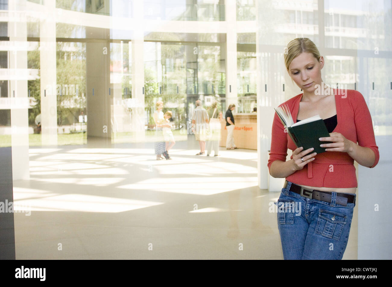 Young woman leaning against glass wall reading book Stock Photo - Alamy