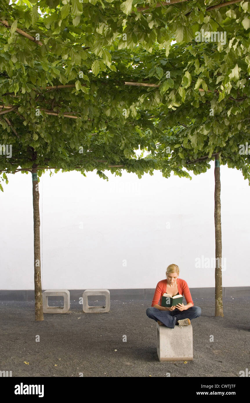Young woman reading book under trees Stock Photo - Alamy