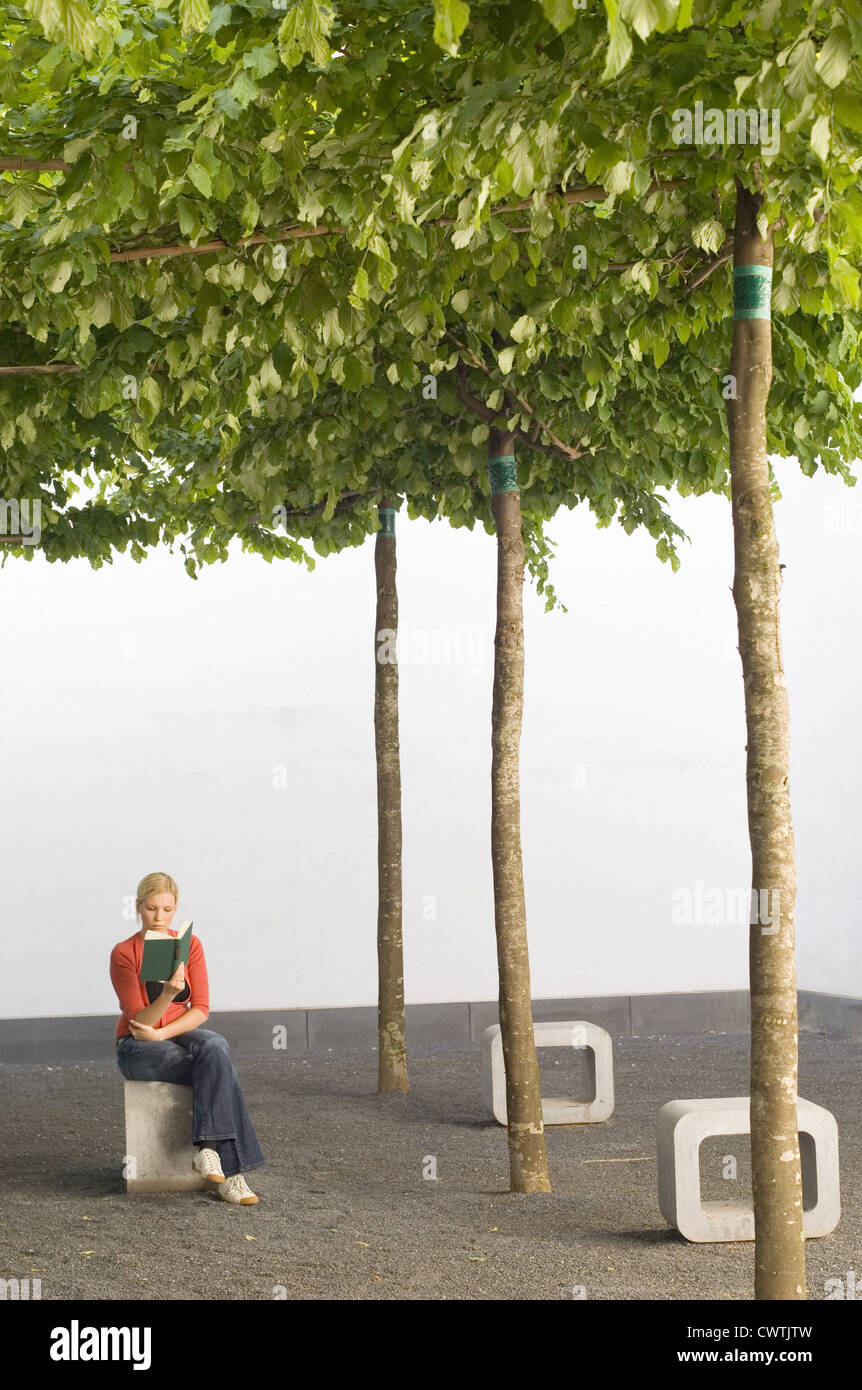 Young woman reading book under trees Stock Photo - Alamy