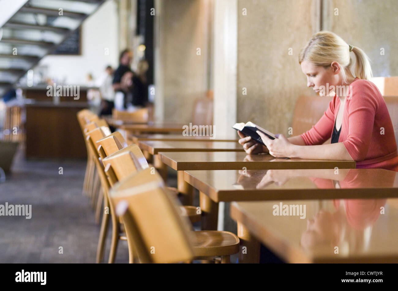 Young woman reading book in restaurant Stock Photo - Alamy