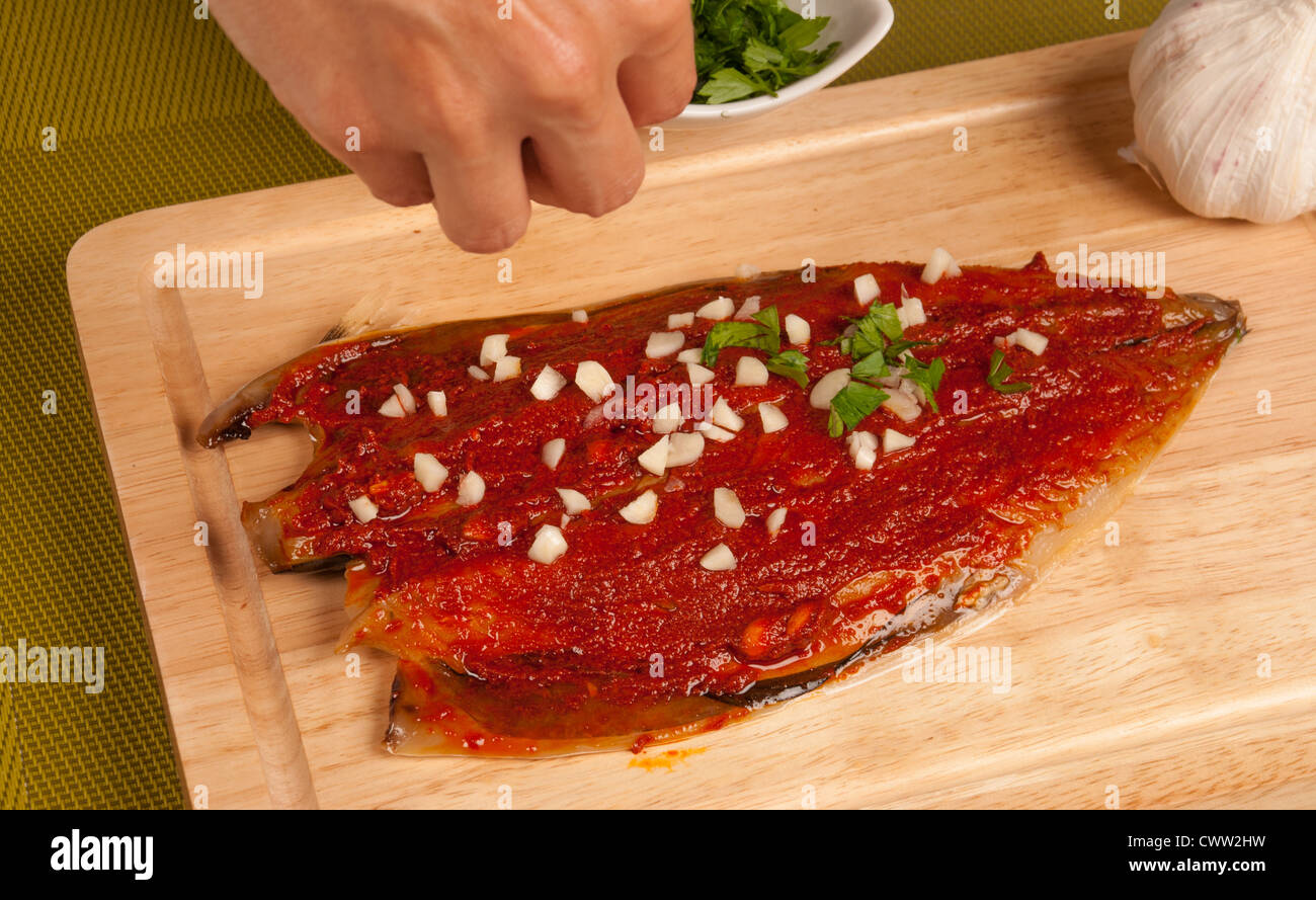 Marinated mackerel being sprinkled with garlic and parsley Stock Photo ...