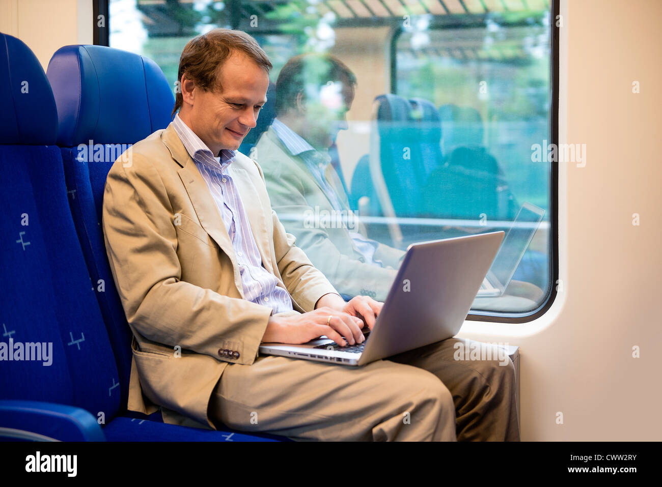 Businessman, traveling with a laptop on his lap in a train, commuting ...