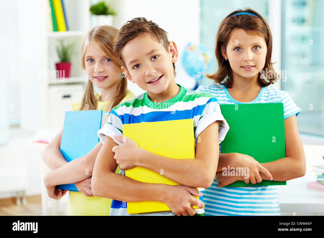 Portrait of happy classmates with books looking at camera in classroom ...