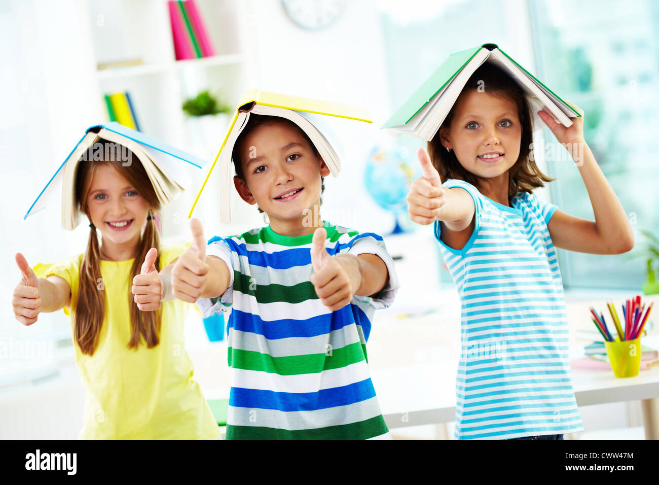 Portrait of happy classmates with books on their heads keeping thumbs ...