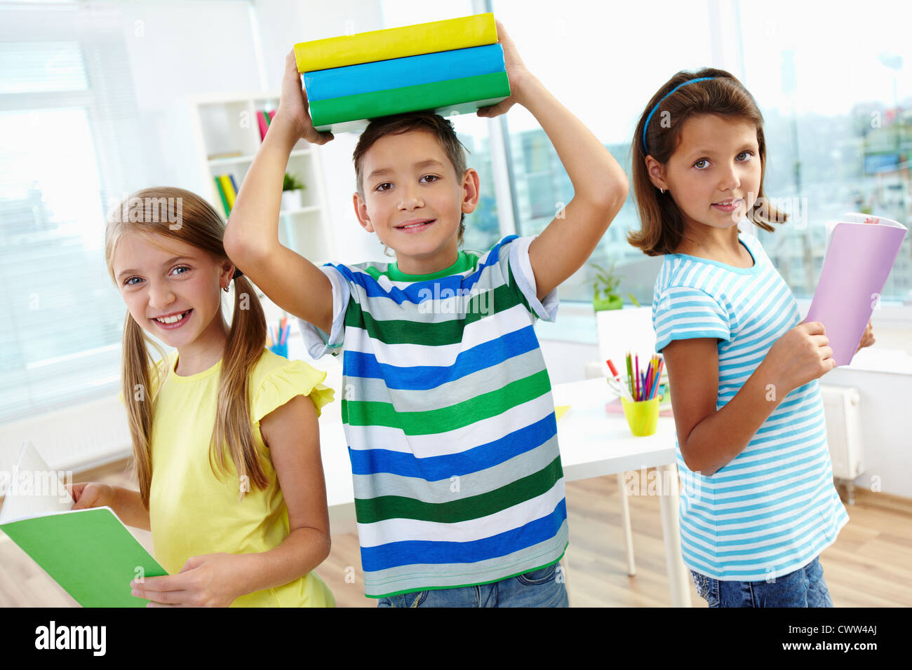 Portrait of happy classmates with books smiling at camera in classroom ...