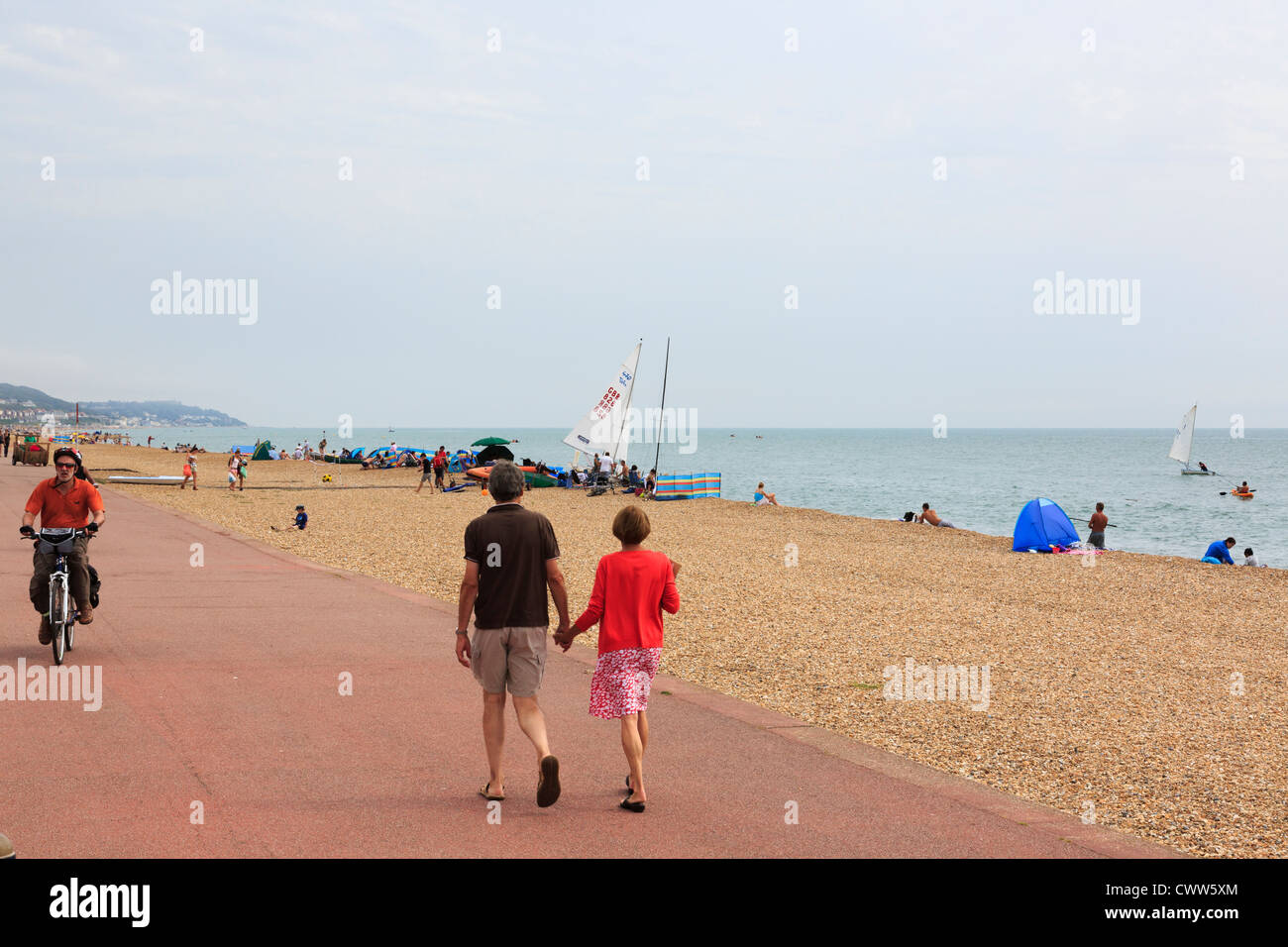 People walking on seafront promenade beside the sea and pebble beach on ...