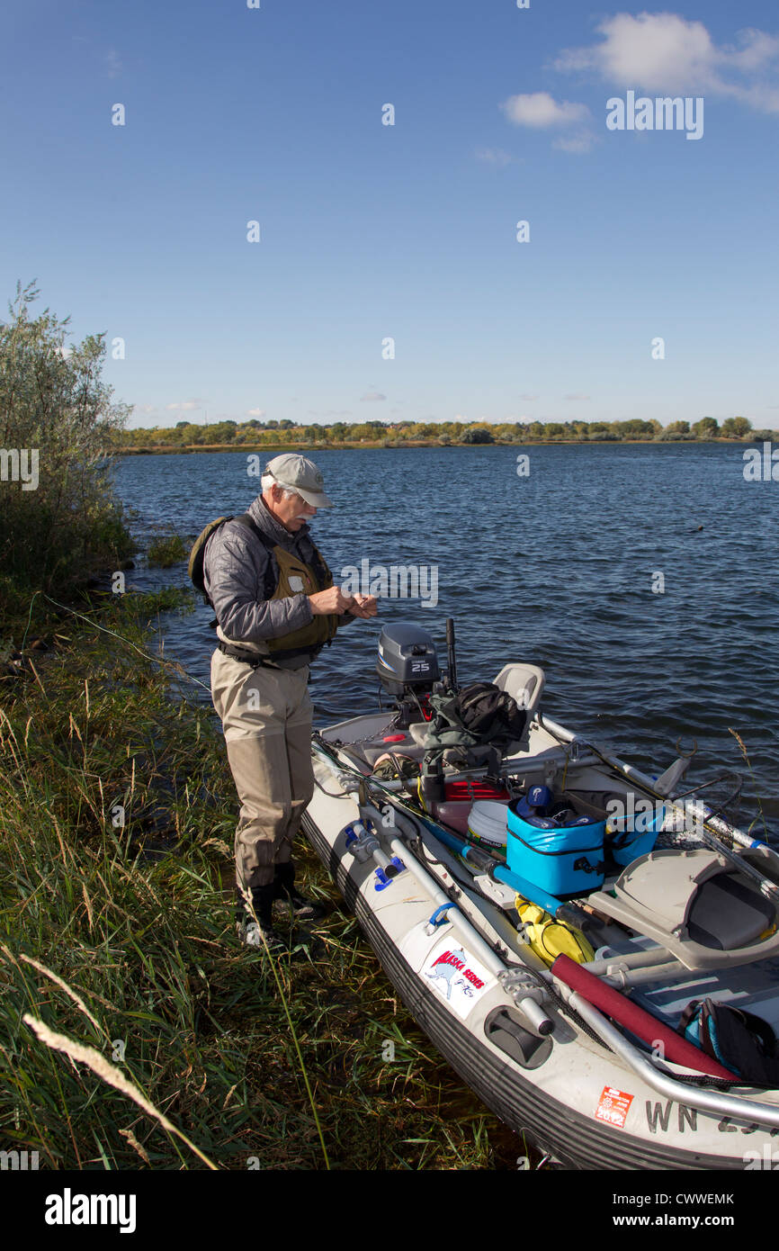 A fisherman rigs up his fly rod while his inflatable jet boat waits ...