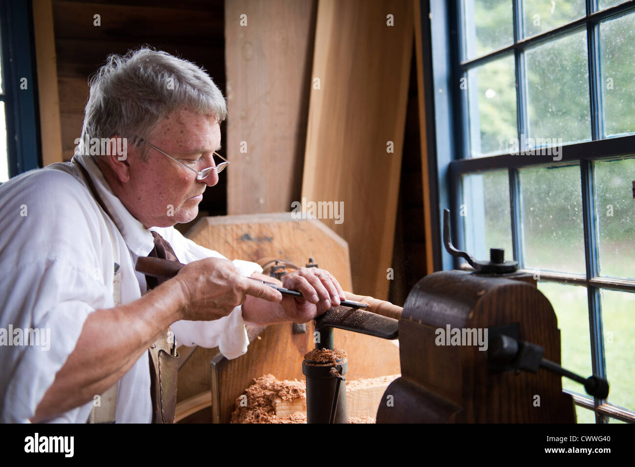Carpenter using a foot operated lathe to turn and carve a piece of wood ...
