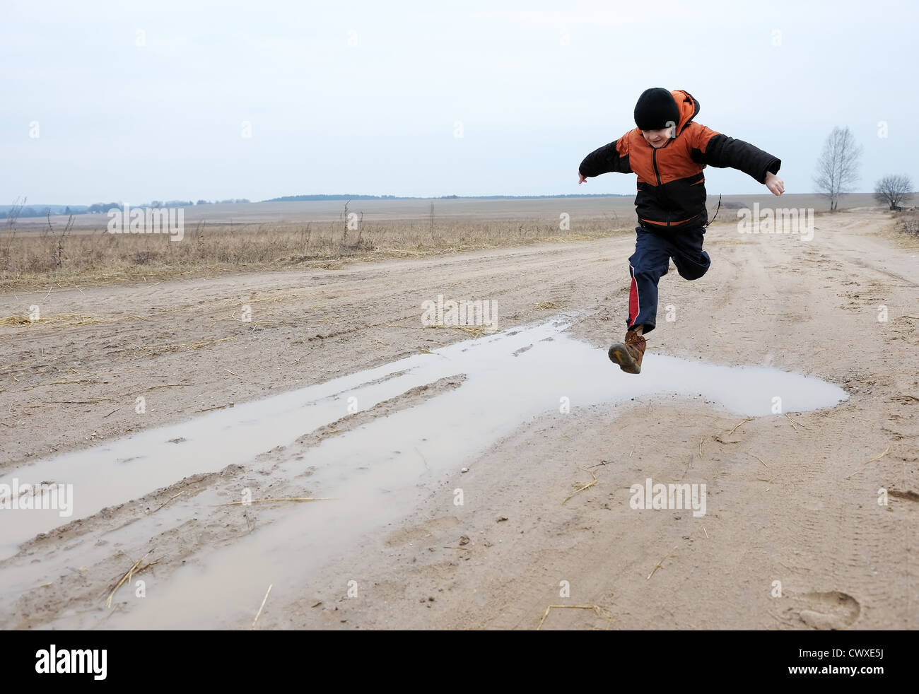 A boy jumps over a puddle on a rural road Stock Photo - Alamy