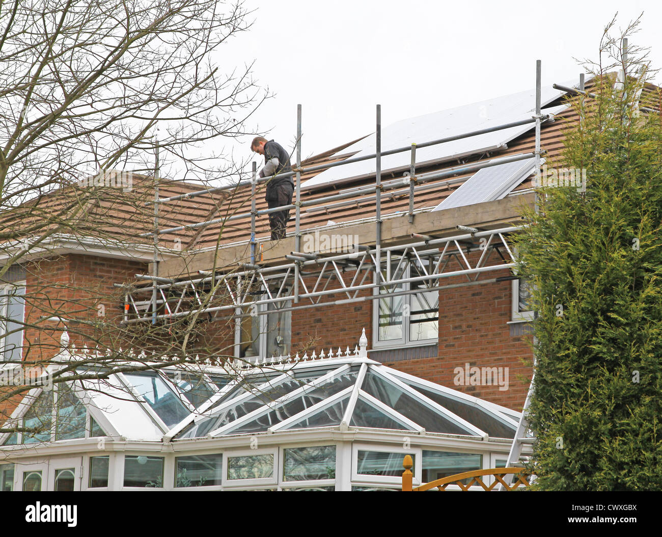A technician standing on scaffolding fitting solar panels to a domestic ...