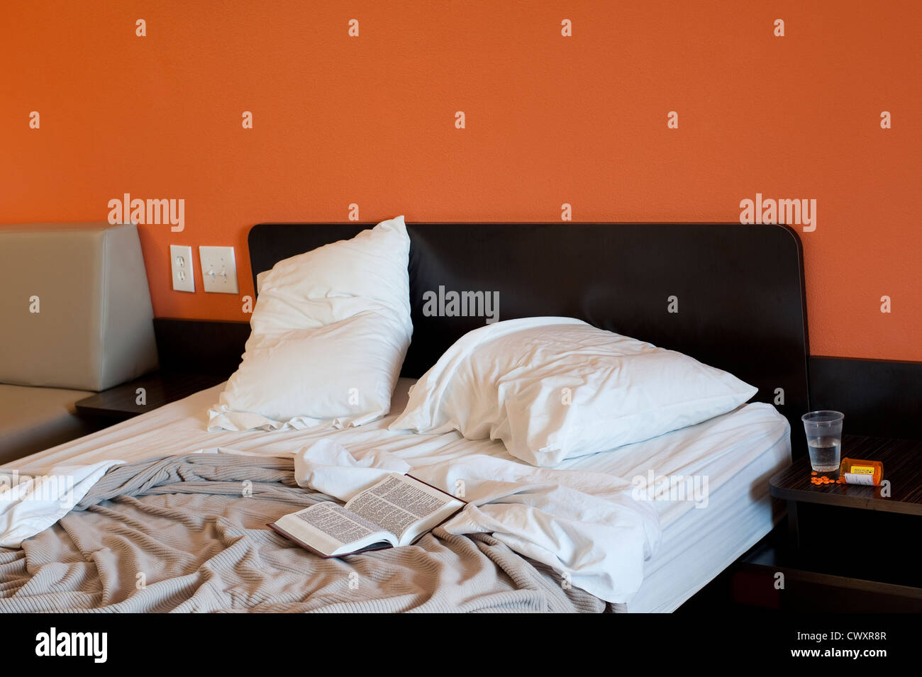 Motel room with messy bed and medications pill bottles on side table ...