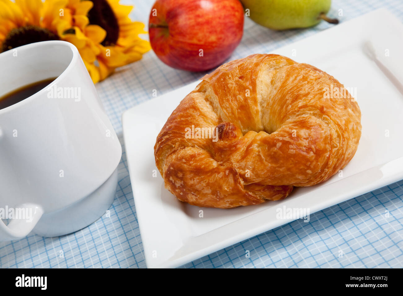 A French croissant with a mug of coffee and apples on a blue check ...