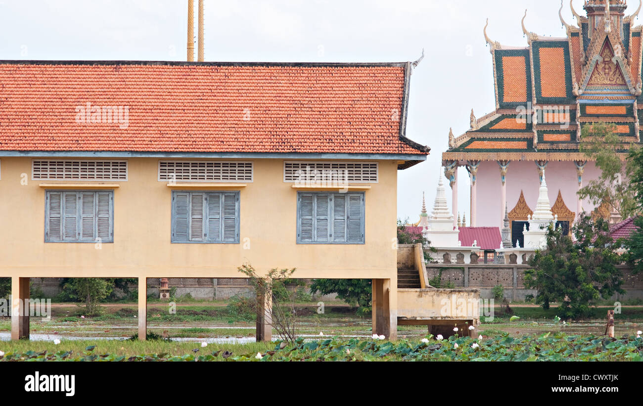 School building on stilts in a pond with lotus flowers and a temple in ...