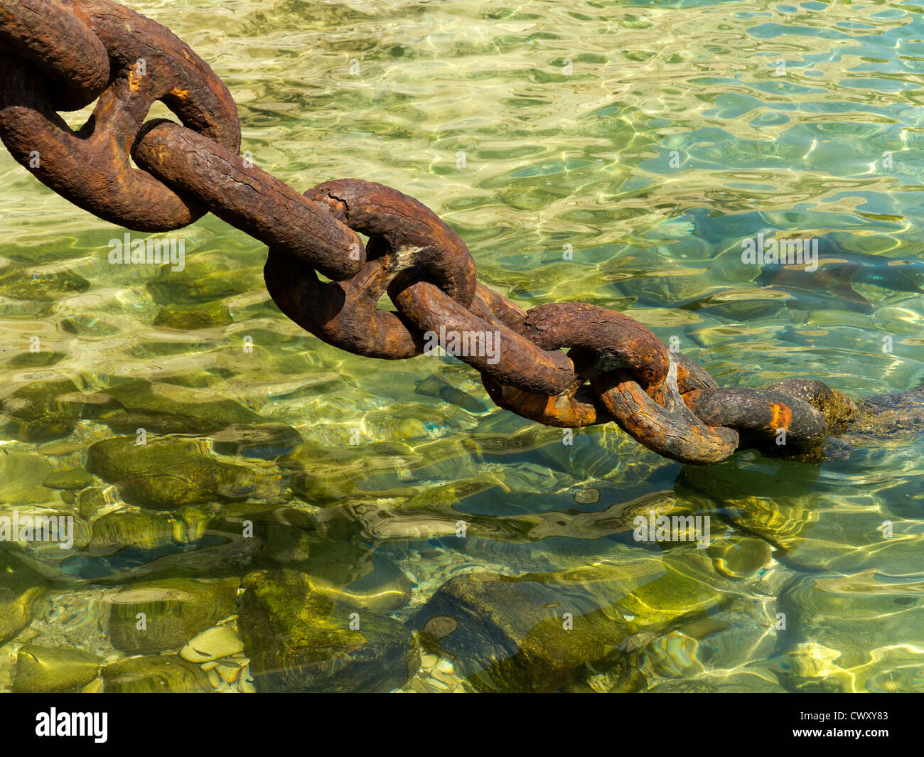 Close up of large rusted anchor chain links entering shallow water ...