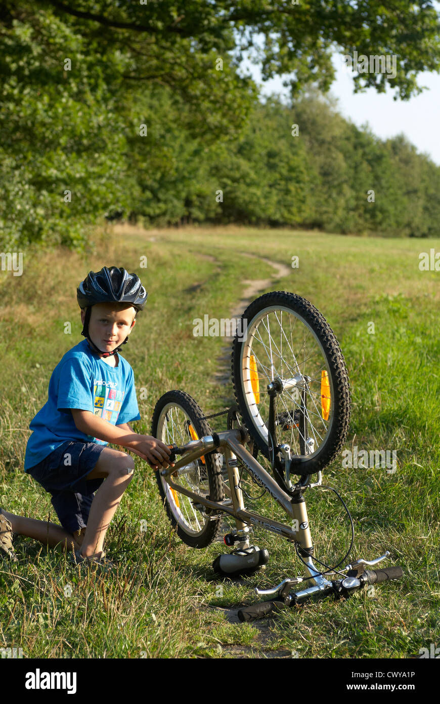 Child blond boy examining and fixing his bicycle outside summer Stock ...