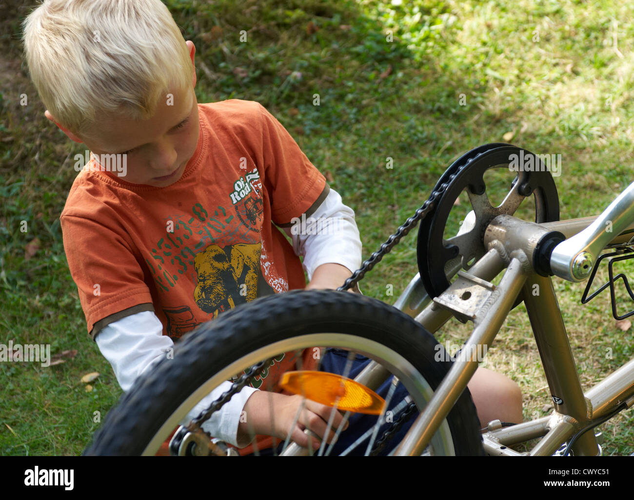 Child blond boy examining and fixing his bicycle outside summer Stock ...