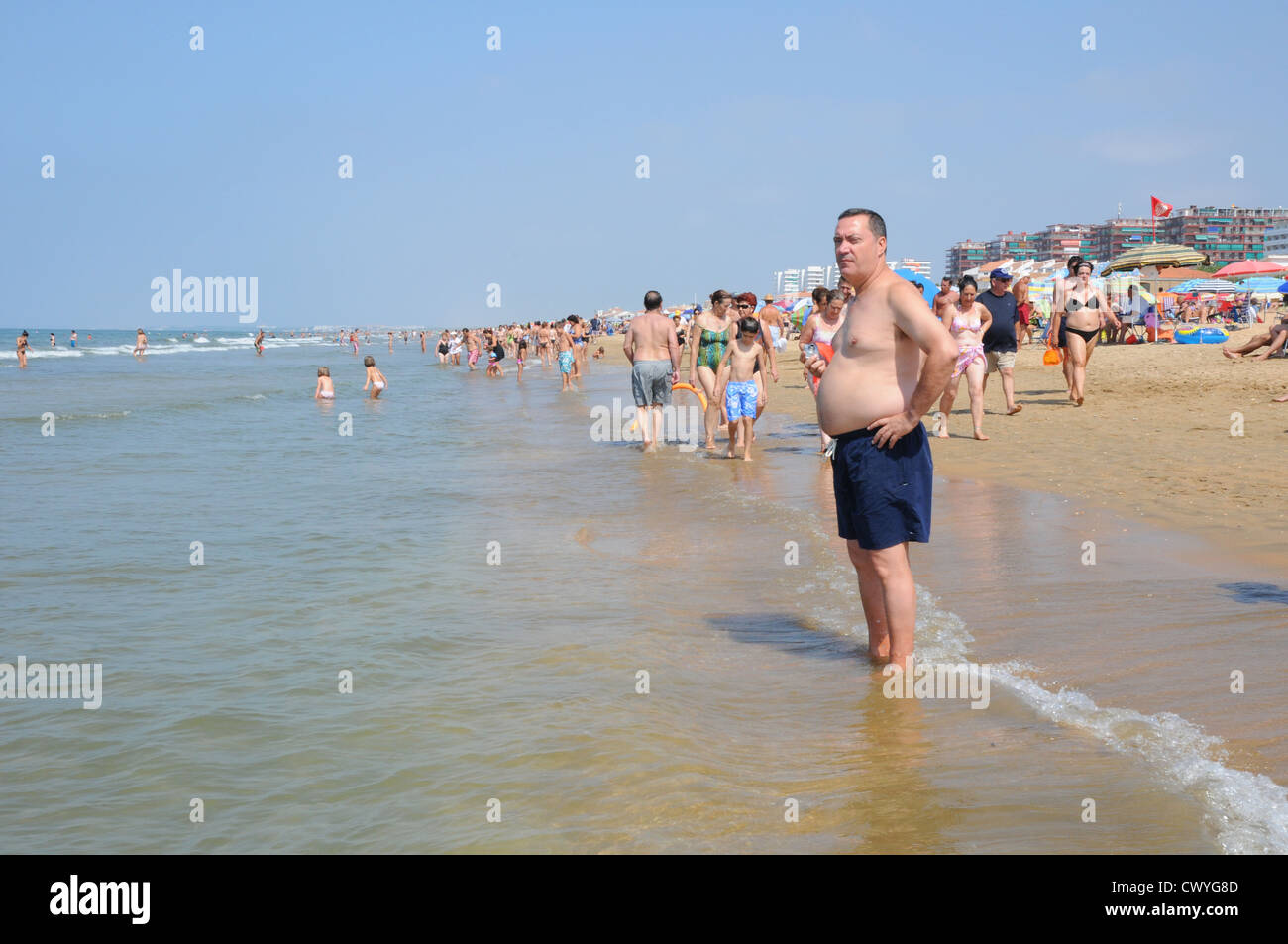 Man with paunch and trunks standing at water's edge in front of crowds ...