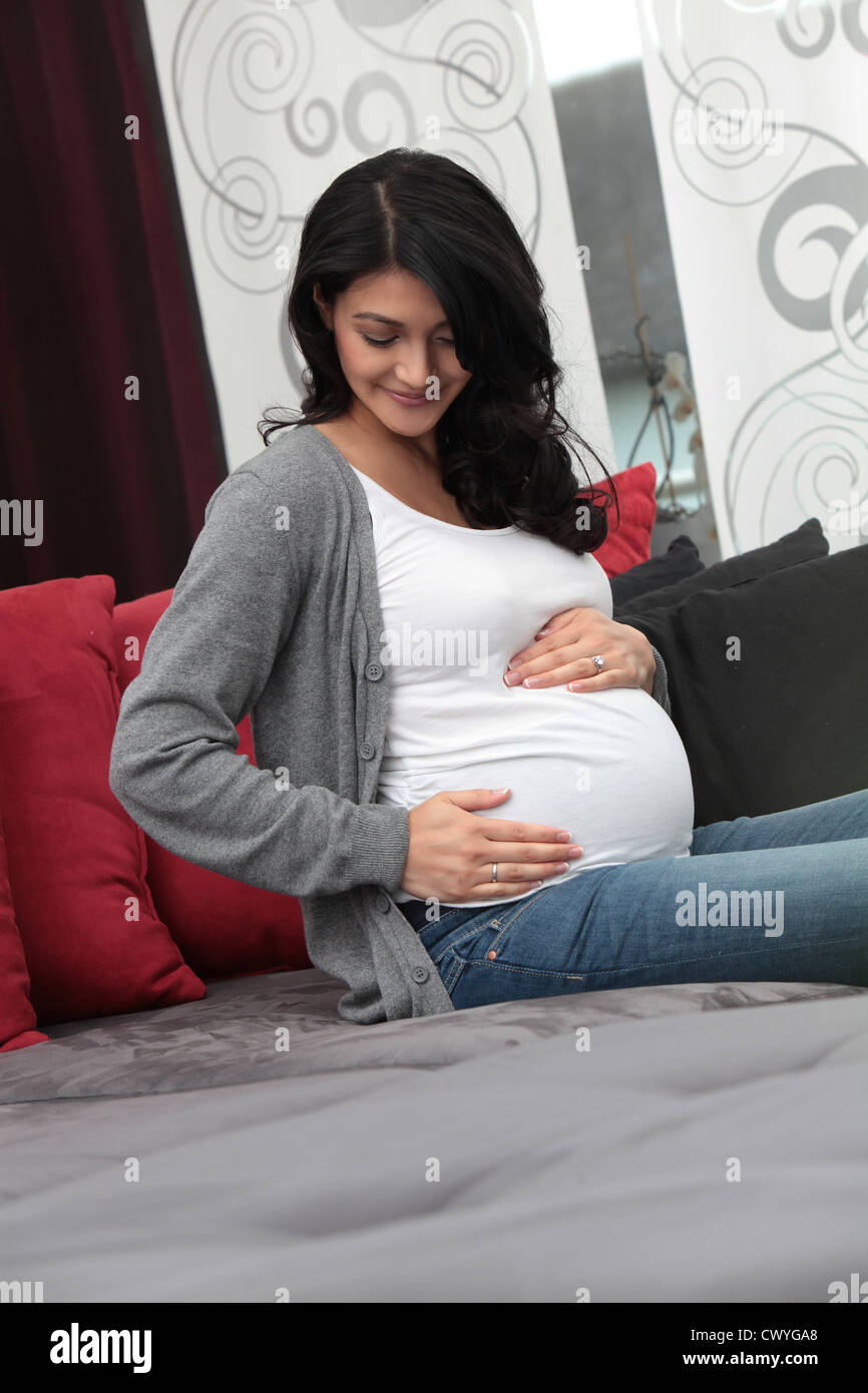 Pregnant woman on couch holding her belly Stock Photo - Alamy