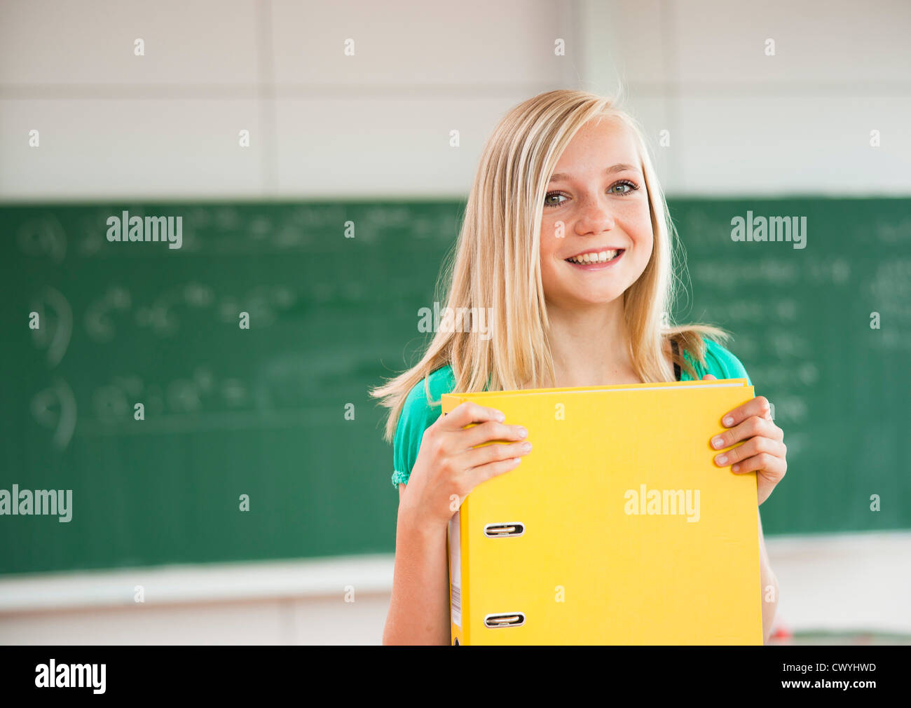 Smiling teenage girl in classroom holding file folder, portrait Stock ...