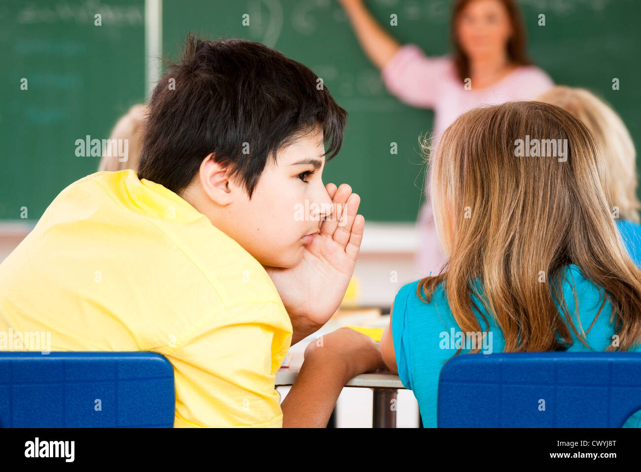 Boy whispering to girl in classroom Stock Photo - Alamy