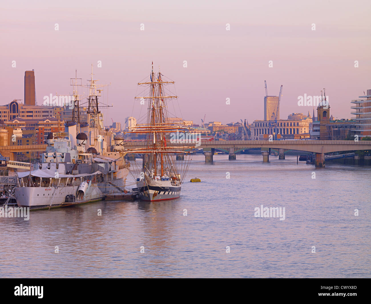 HMS Belfast with a tall ship moored alongside at dawn, London UK Stock ...