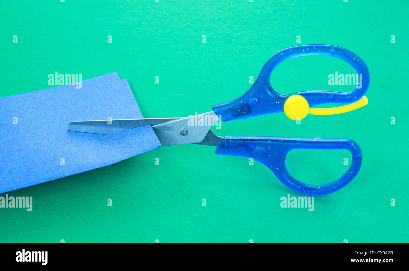 Child's scissors cutting blue craft paper on a green paper background ...
