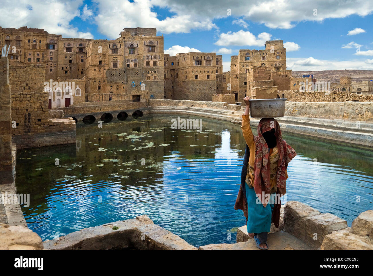 A woman, dressed in traditional clothes, uses a public fountain basin ...