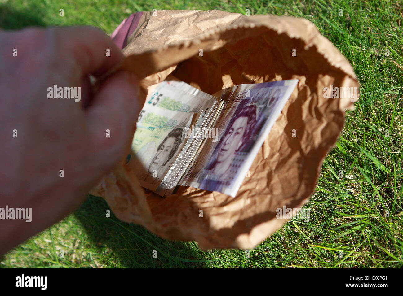 a hand holding a brown paper bag containing sterling notes and lying on ...