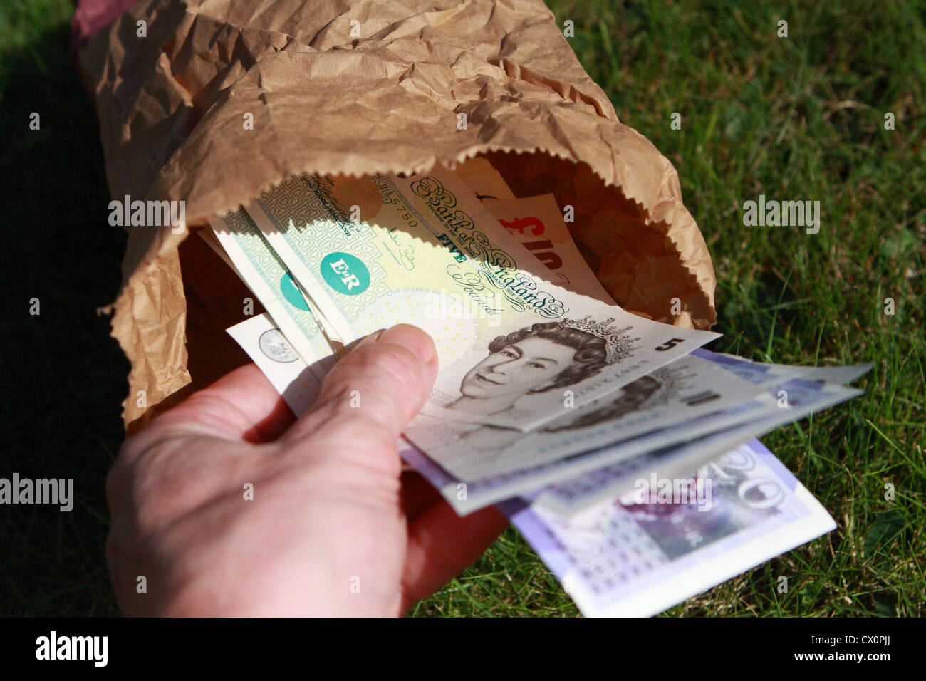 a hand pulling sterling notes out of a brown paper bag lying on grass ...