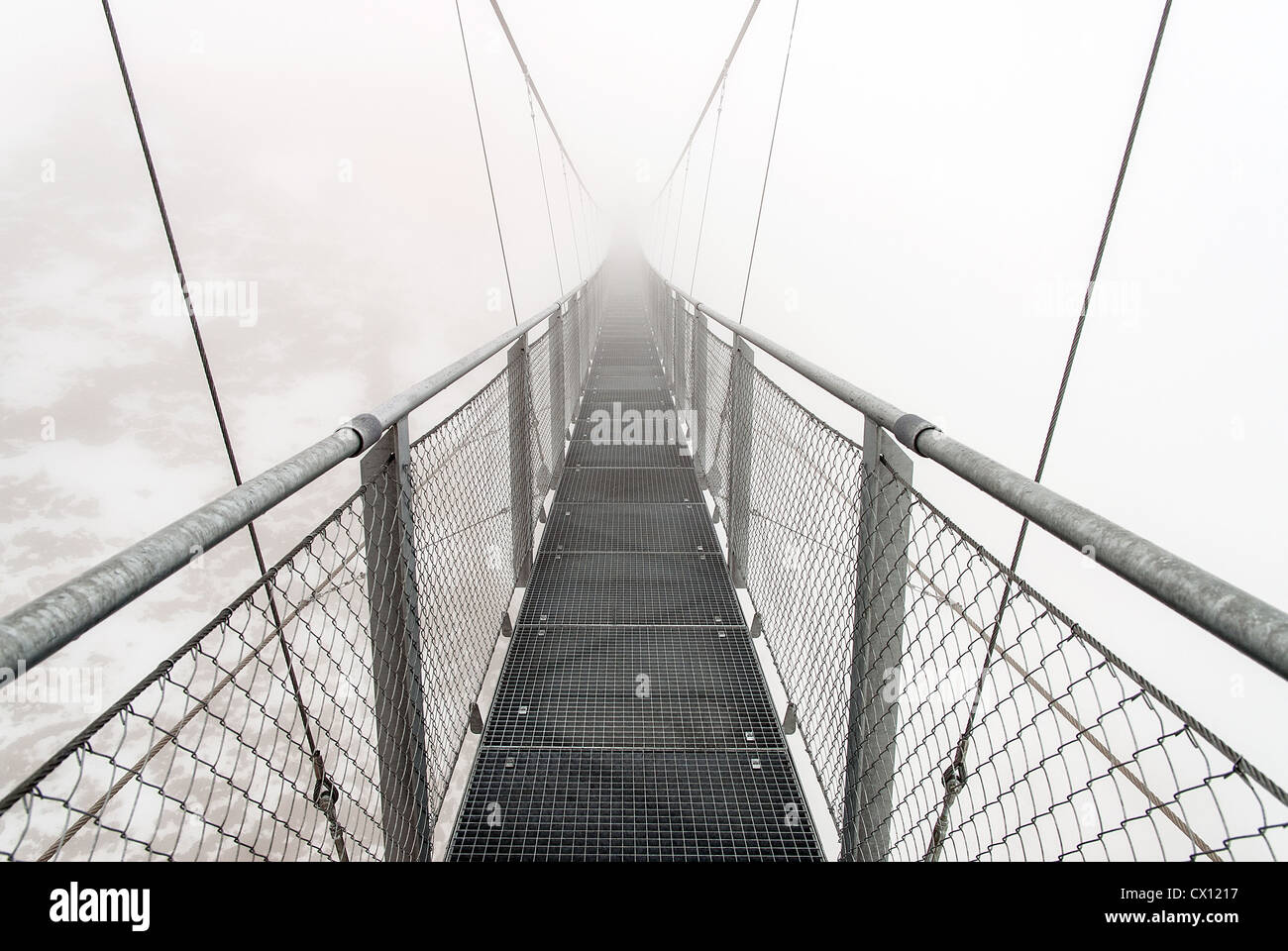 A metallic bridge for hikers in snowy Austrian Alps during a foggy day ...