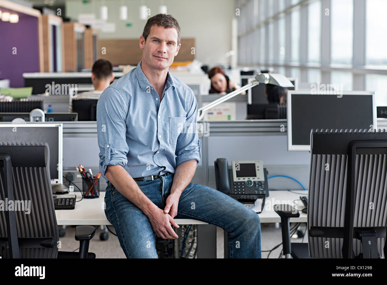 Portrait of man sitting on desk Stock Photo - Alamy