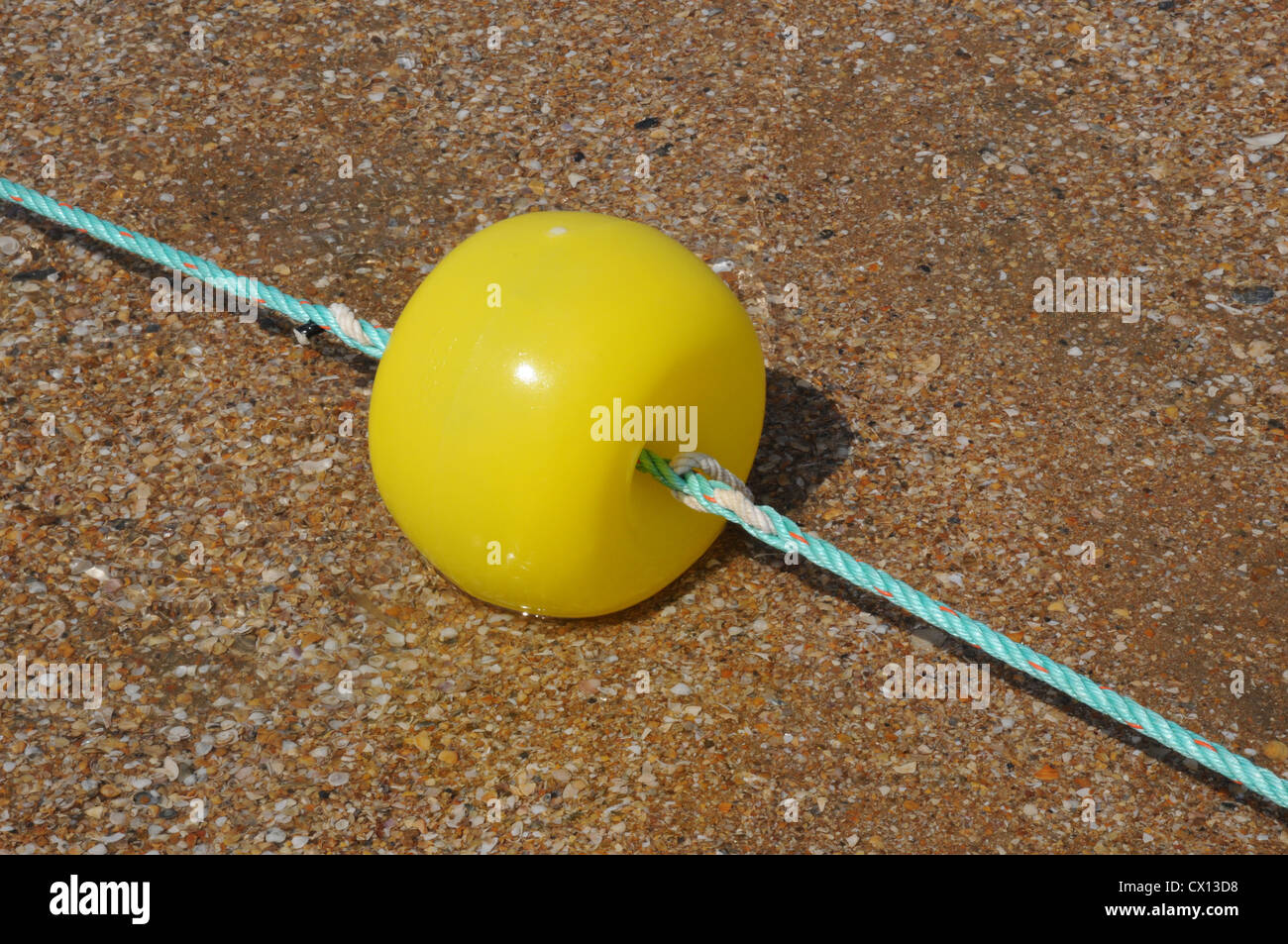 Yellow plastic float with blue rope on shingle, seaside, Costa de la ...