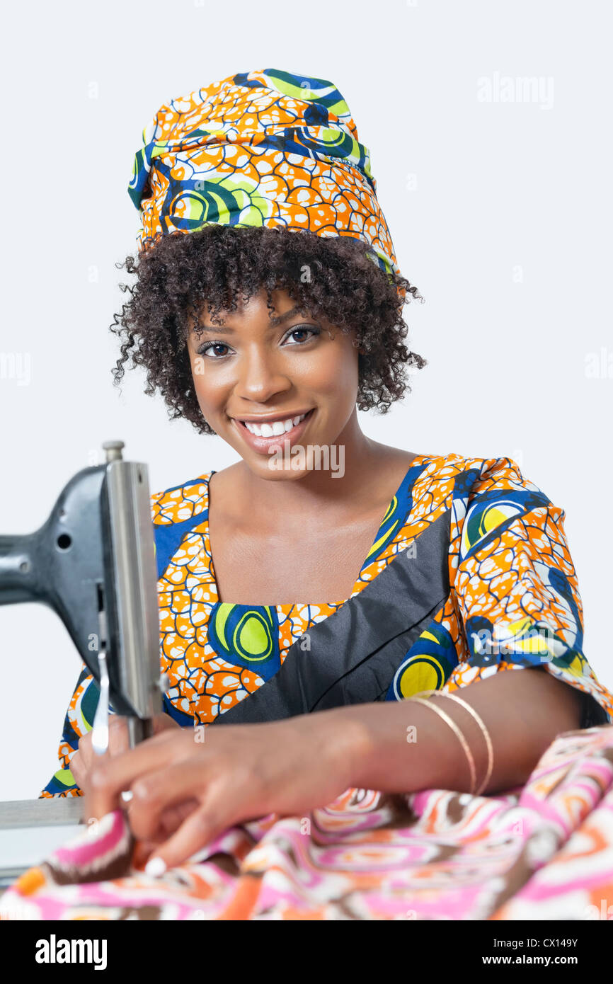 Portrait of an African American woman using sewing machine over gray ...