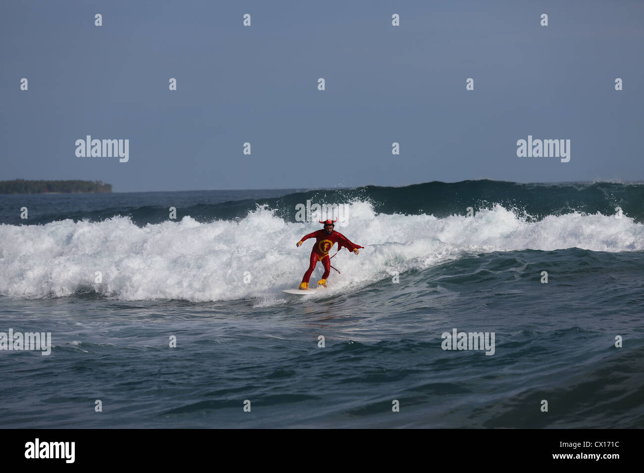 Surfer dressed in red devil super hero costume surfing a wave in Krui ...