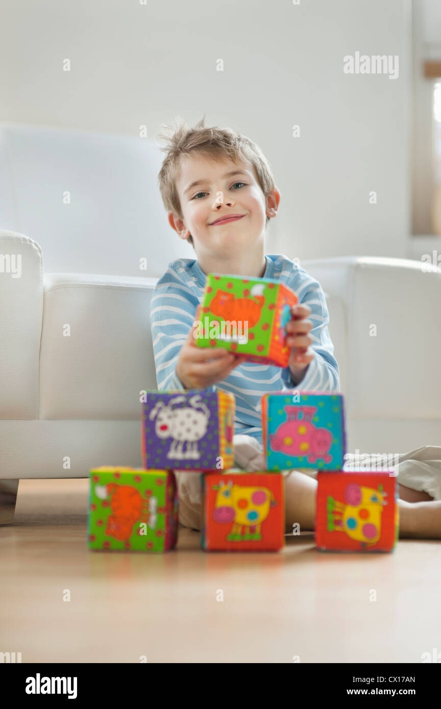 Portrait of cute little boy stacking blocks while sitting on floor ...