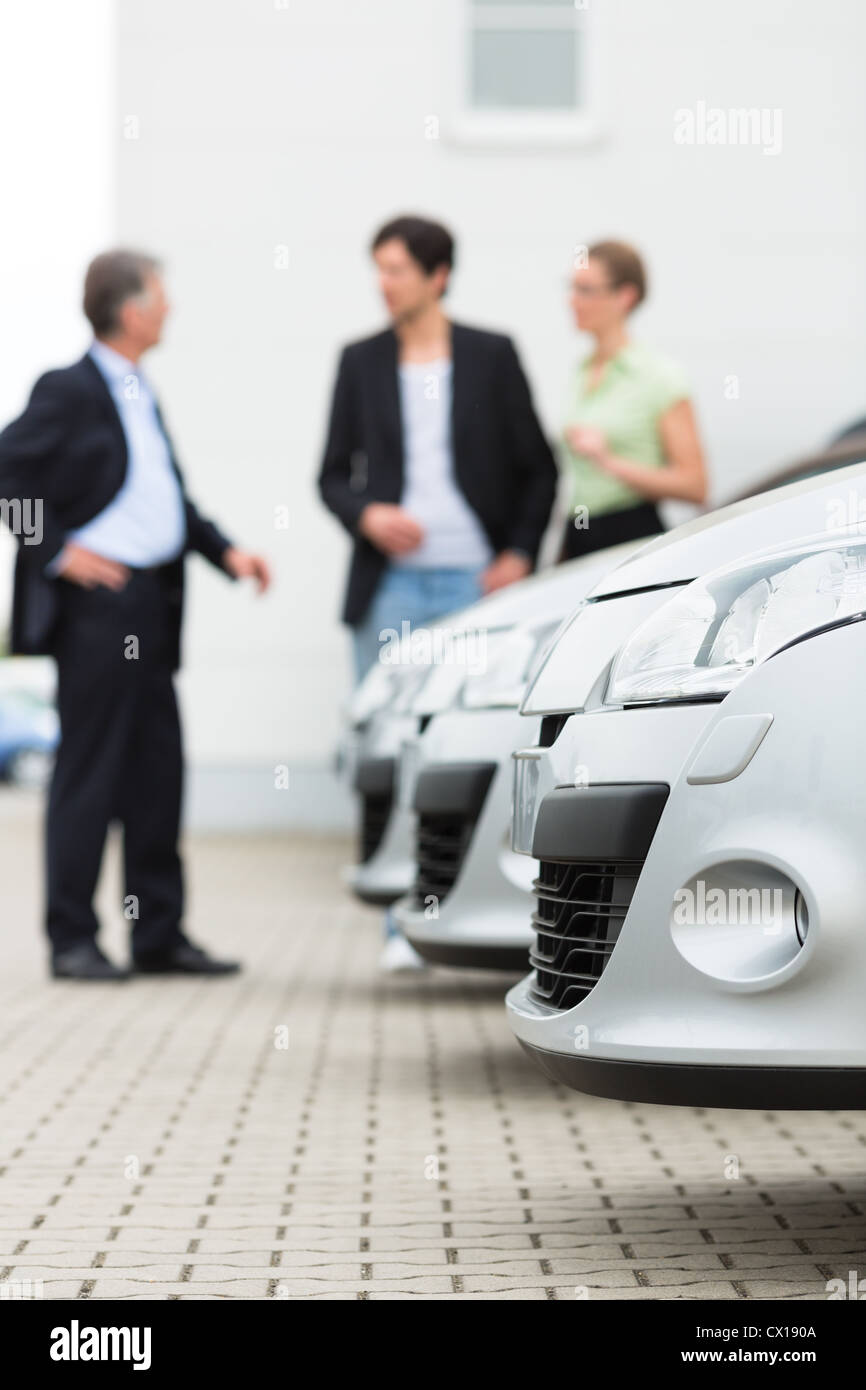 Two men man and one woman stand behind a row of silver-metallic cars on ...