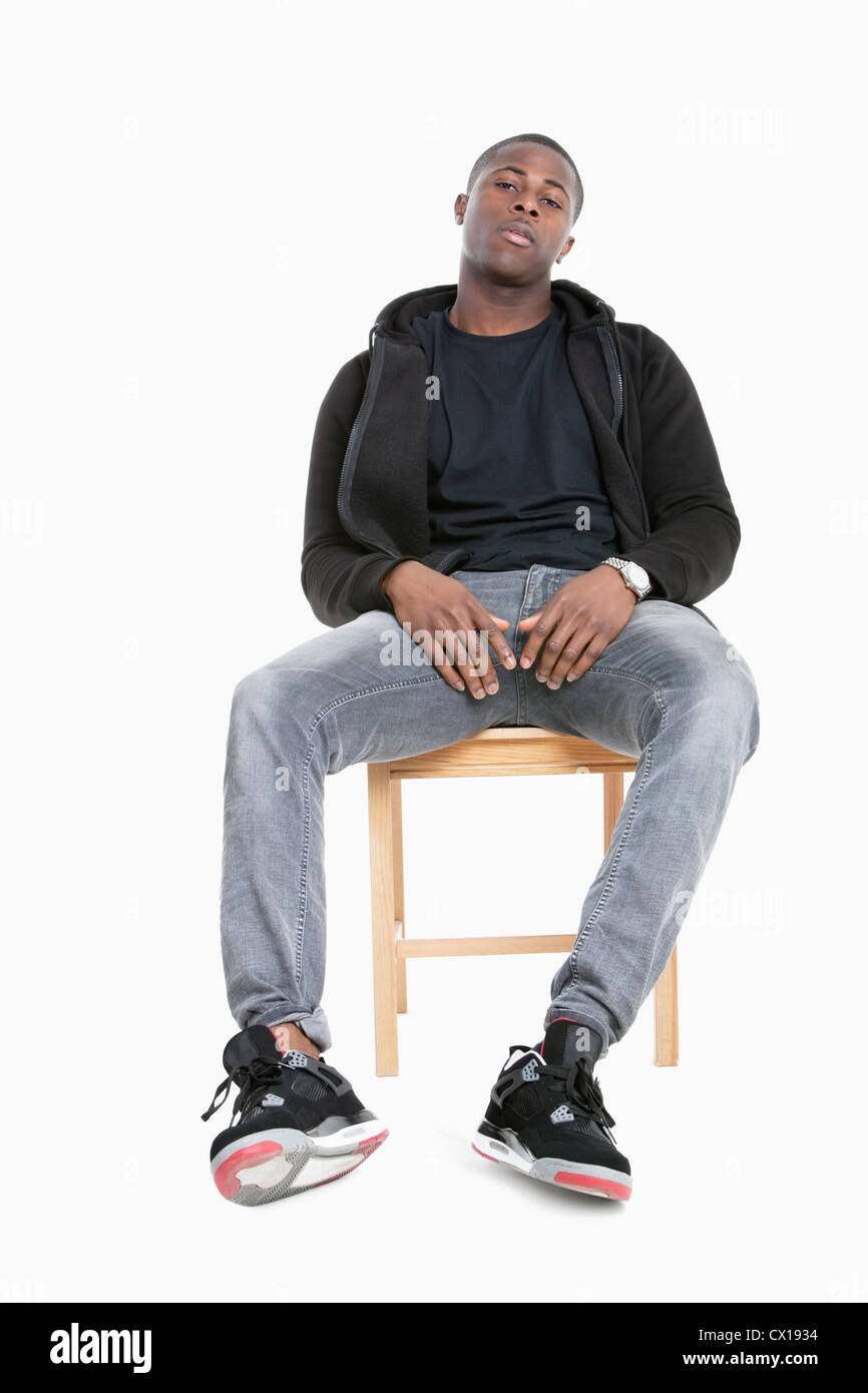 Portrait of a trendy African American man sitting on chair over gray ...