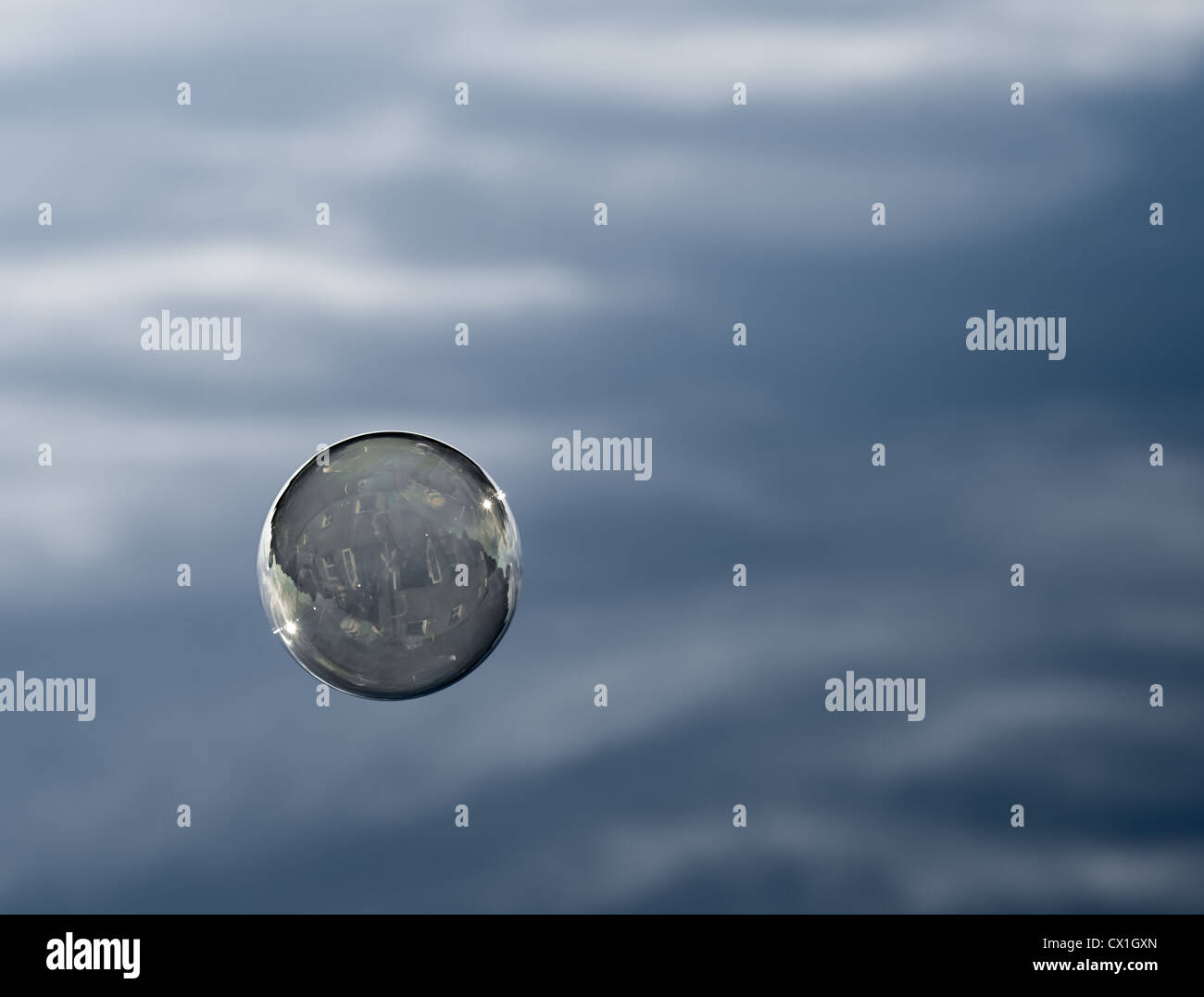 A single soap bubble, reflecting a cottage below floats in a cloudy sky ...