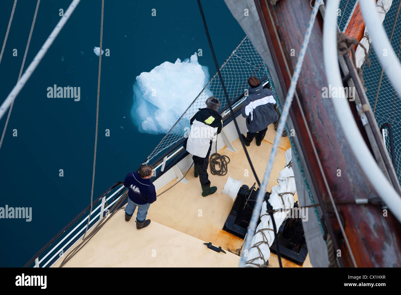 Tourists on board of sailing ship looking at passing melting iceberg ...