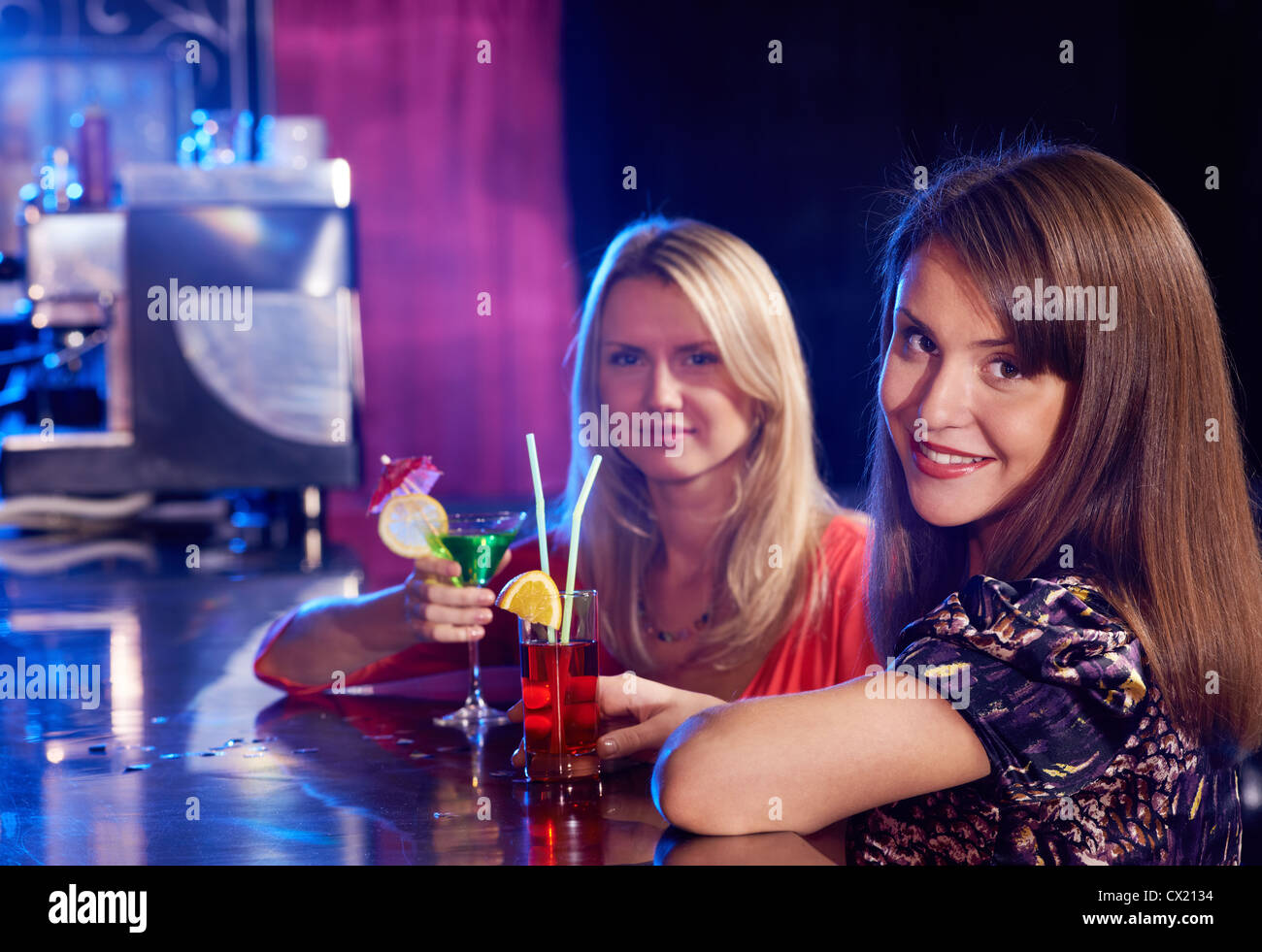 Portrait of happy girlfriends holding glasses with cocktails in bar ...