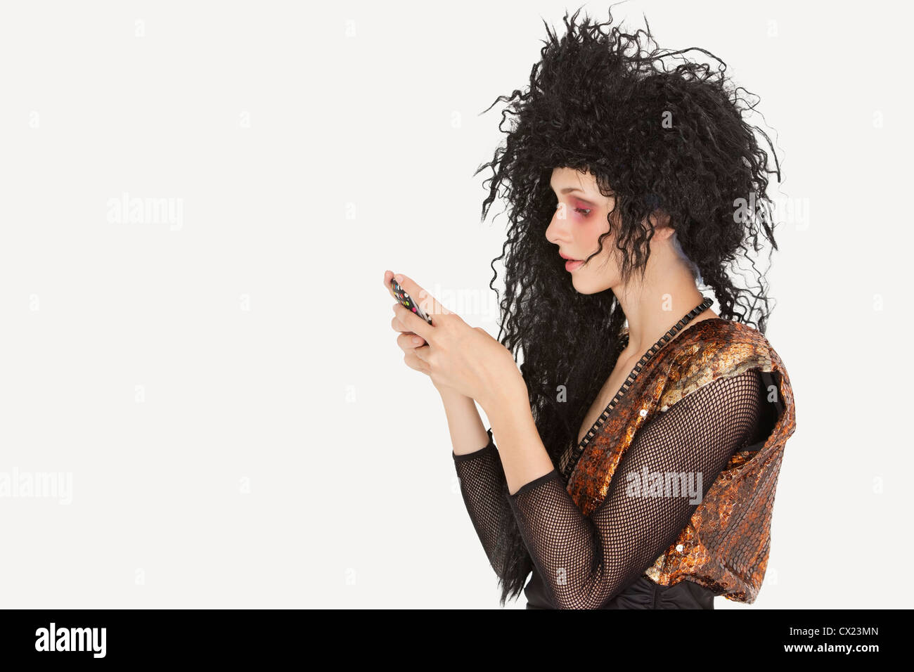 Side view of young Goth woman with teased hair texting on mobile phone ...